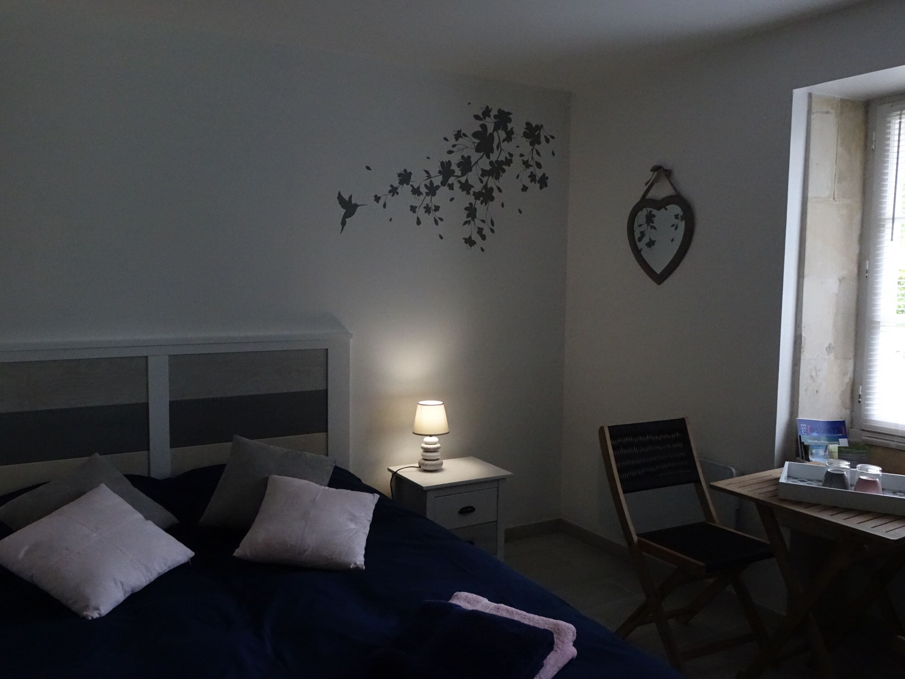 Quarto com cama, mesa de cabeceira com abajur, uma cadeira, escrivaninha e janela com persianas.