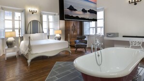 Quarto com uma cama grande, uma banheira e televisão fixada na parede.