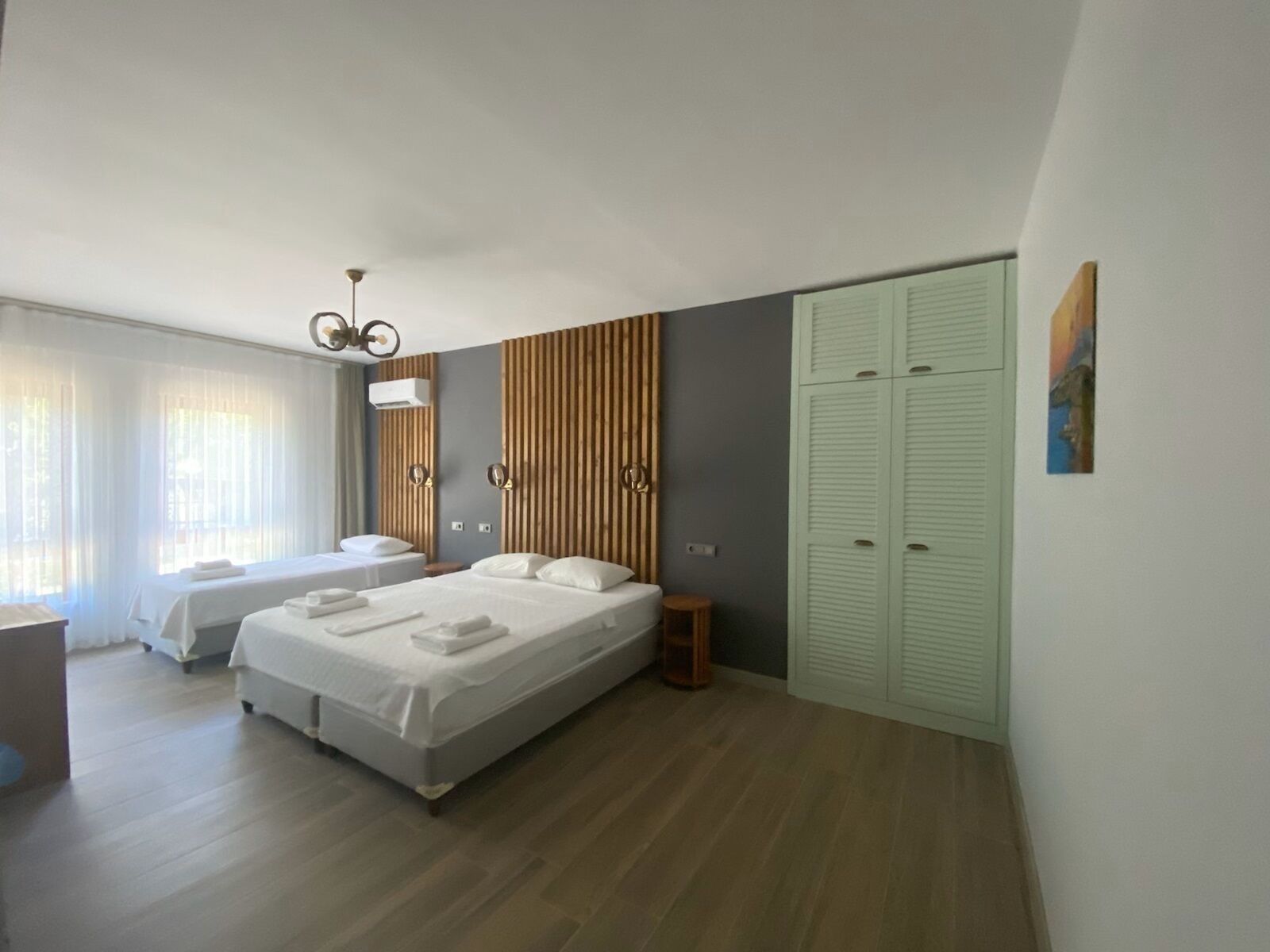 Quarto moderno com duas camas, um painel de parede em madeira, um guarda-roupa e uma pequena mesa de cabeceira.