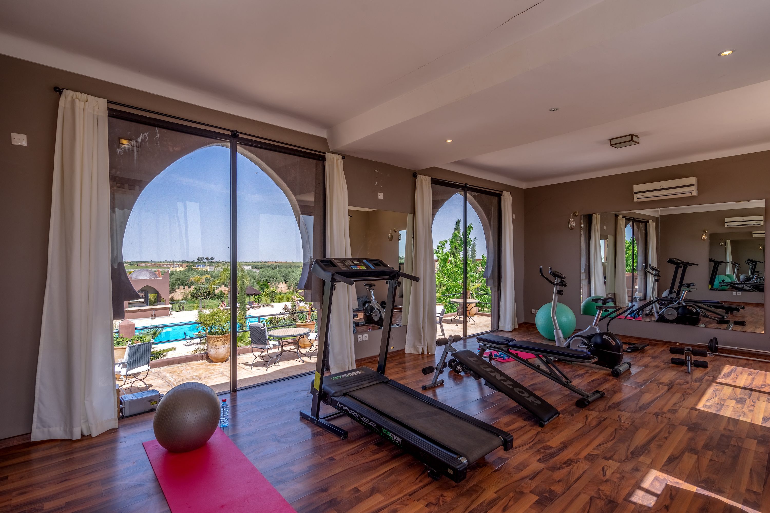 Quarto espaçoso com uma janela grande, esteira e equipamentos de ginástica.