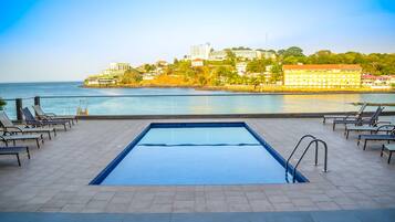 Piscina com espreguiçadeiras e vista para a paisagem urbana costeira.