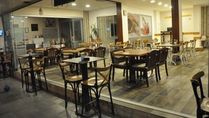 Um restaurante com várias mesas e cadeiras, uma televisão presa à parede e uma escada que leva a um andar superior.