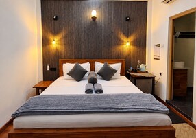 Cama bem arrumada com travesseiros, cabeceira de madeira e mesa de cabeceira com abajur e garrafa.