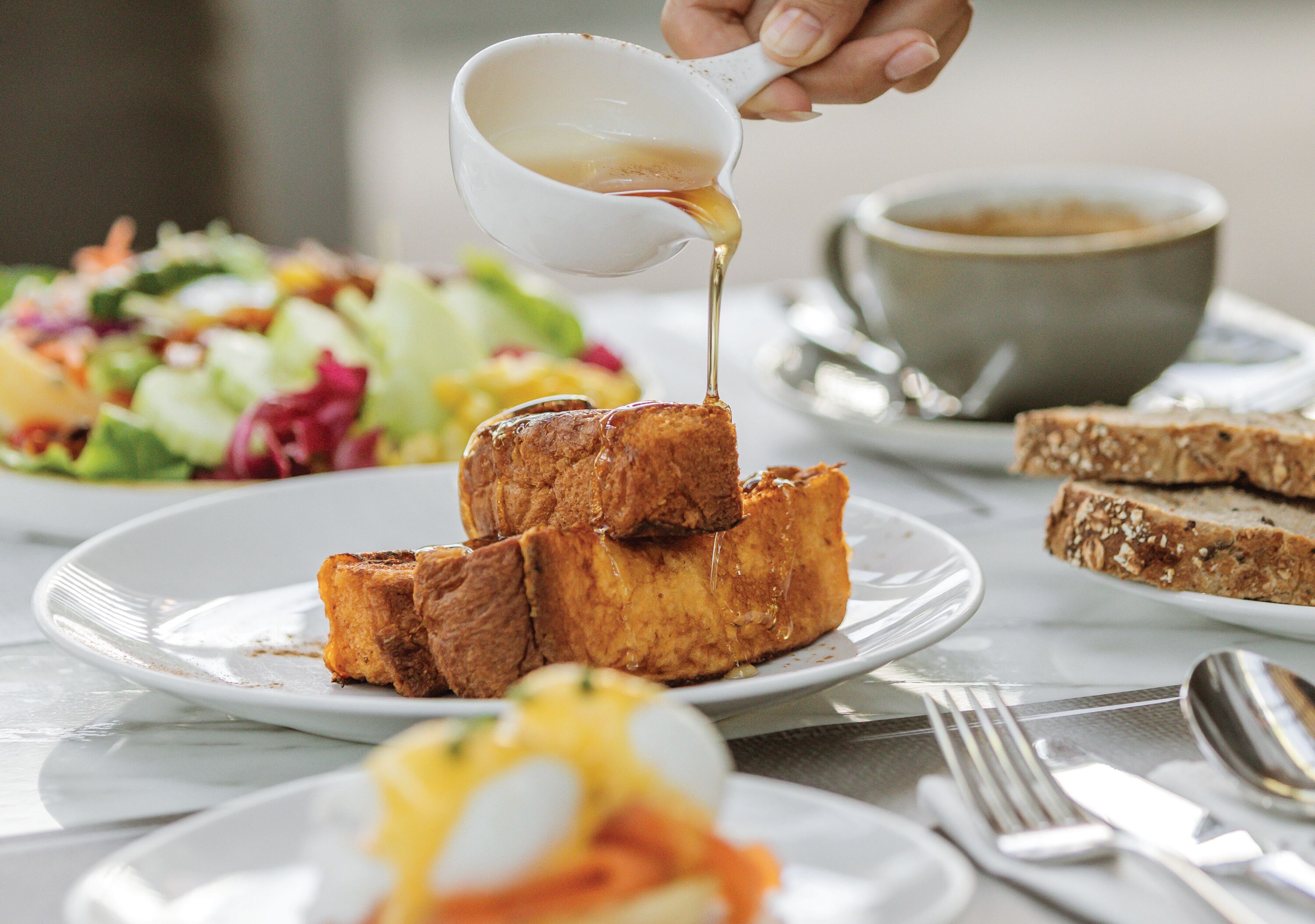 Mesa de café da manhã com torradas, salada e uma xícara de café.