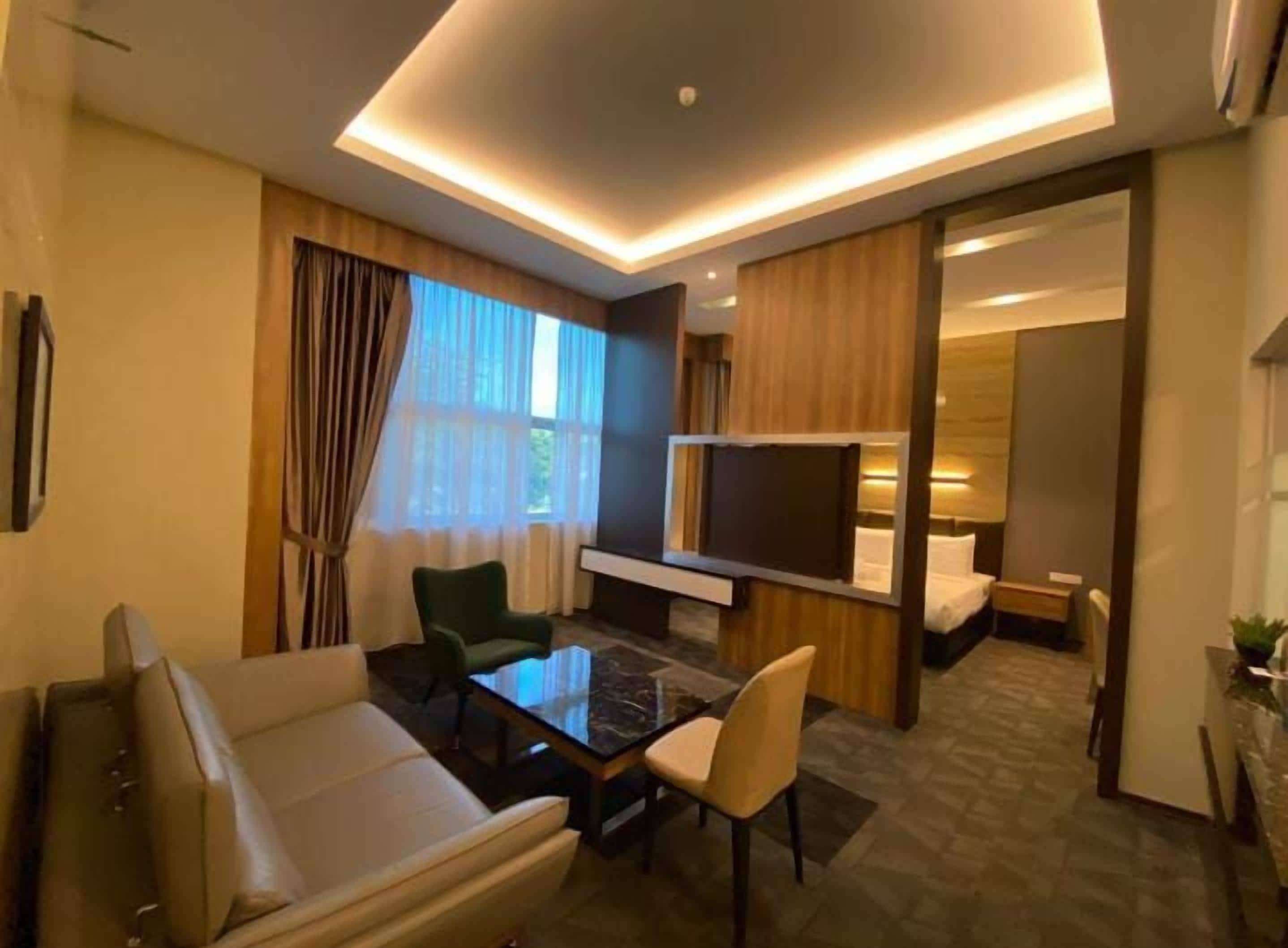 Quarto de hotel com sofá, mesa de jantar, televisão e área de dormir separada.
