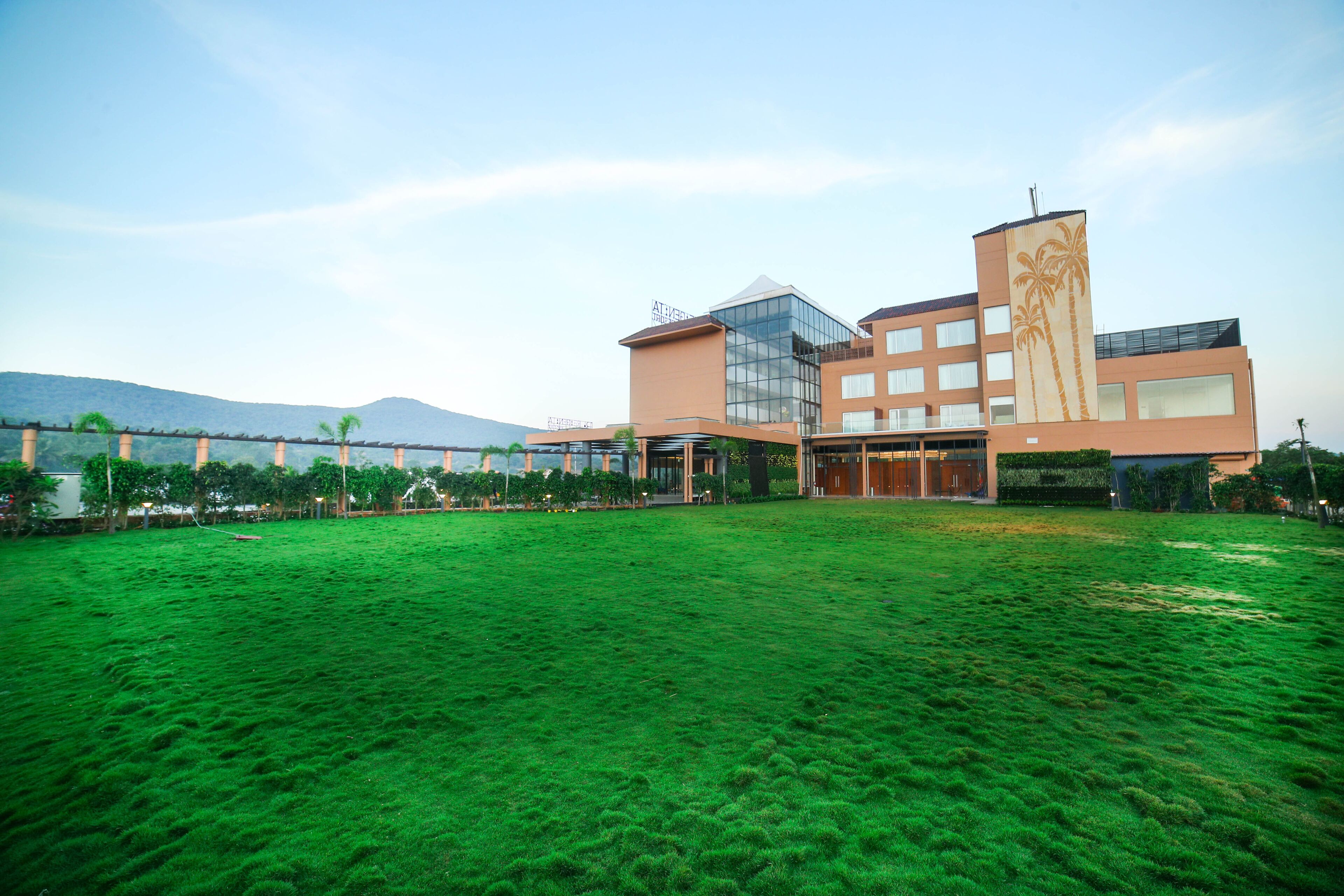 Um hotel moderno com um amplo pátio gramado, vários andares e fachada de vidro marcante.