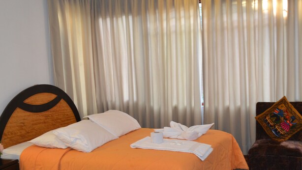 Quarto de hotel com cama, uma cadeira e cortina.