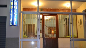 Entrada de um hotel com uma placa indicando "HOSTAL" e uma porta de madeira com painéis de vidro.