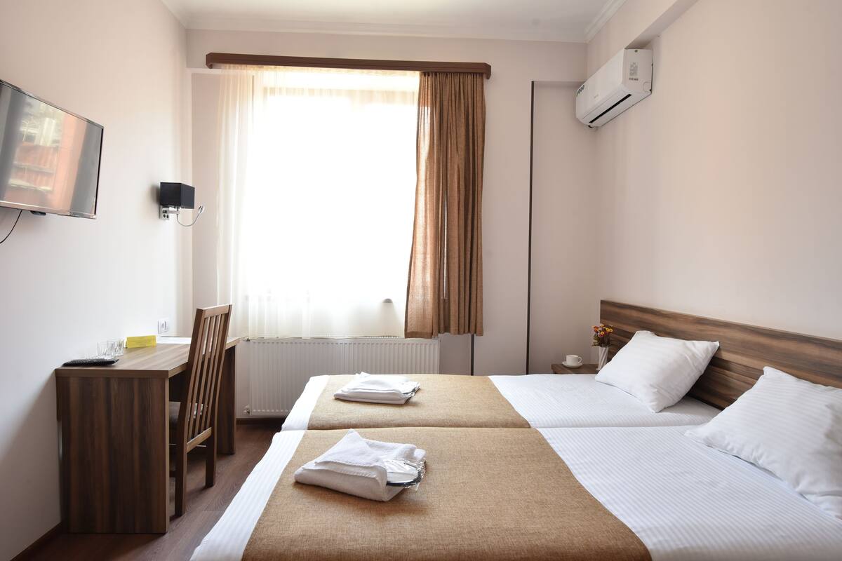 Quarto de hotel com duas camas, uma escrivaninha, uma cadeira, uma televisão e ar condicionado.