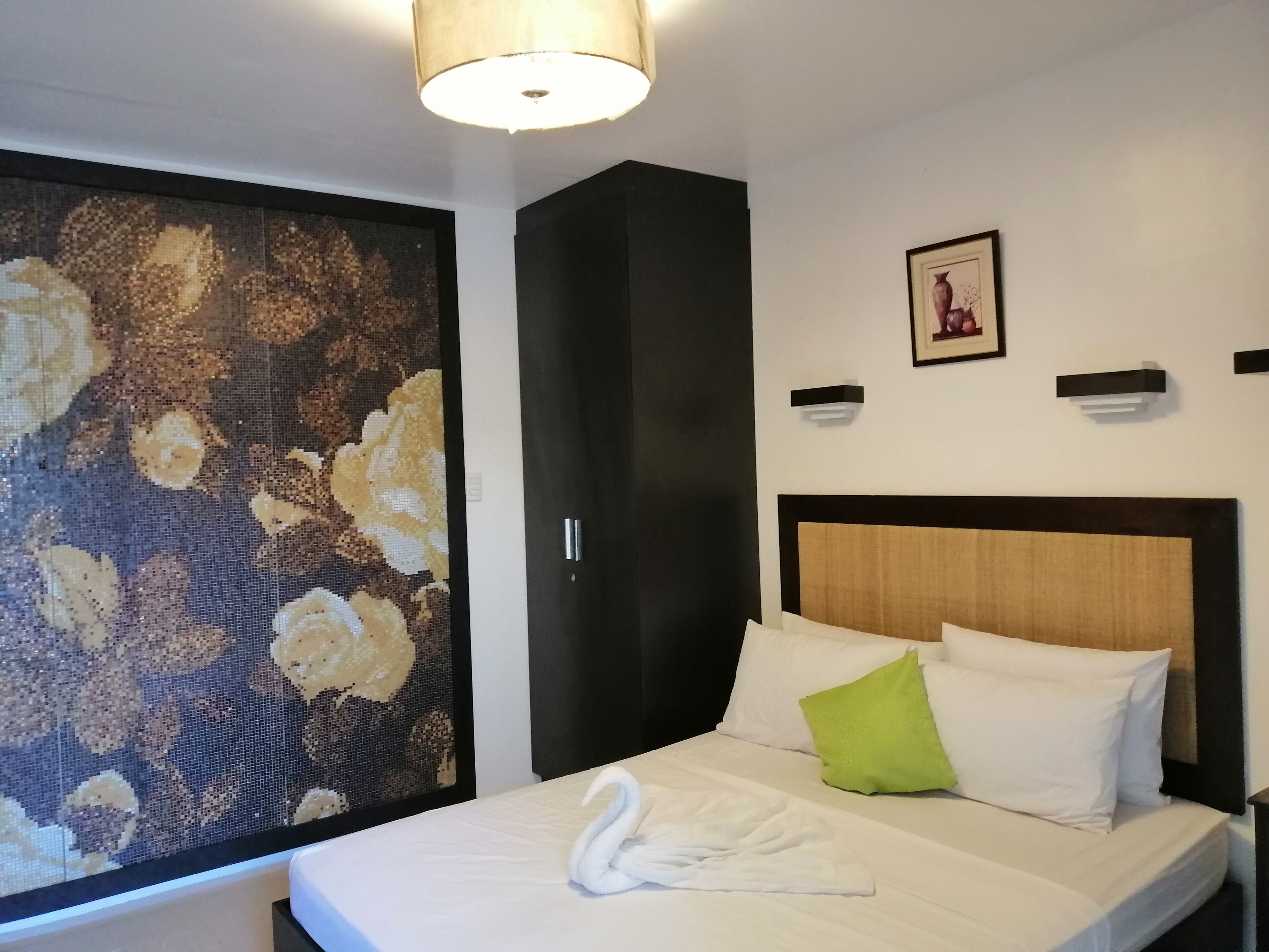 Quarto de hotel com uma cama, uma grande obra de arte floral na parede, um quadro emoldurado e um candeeiro sobre a cama.