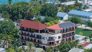 Hotel de vários andares com telhado vermelho, cercado por palmeiras e vista para o oceano.