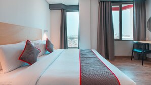 Quarto de hotel com uma cama grande, uma escrivaninha e vista para a cidade pela janela.