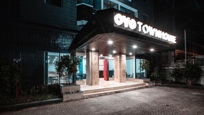 Entrada de hotel com uma placa grande indicando 'OYO TOWNSIDE', uma porta vermelha e um caminho pavimentado até a entrada.