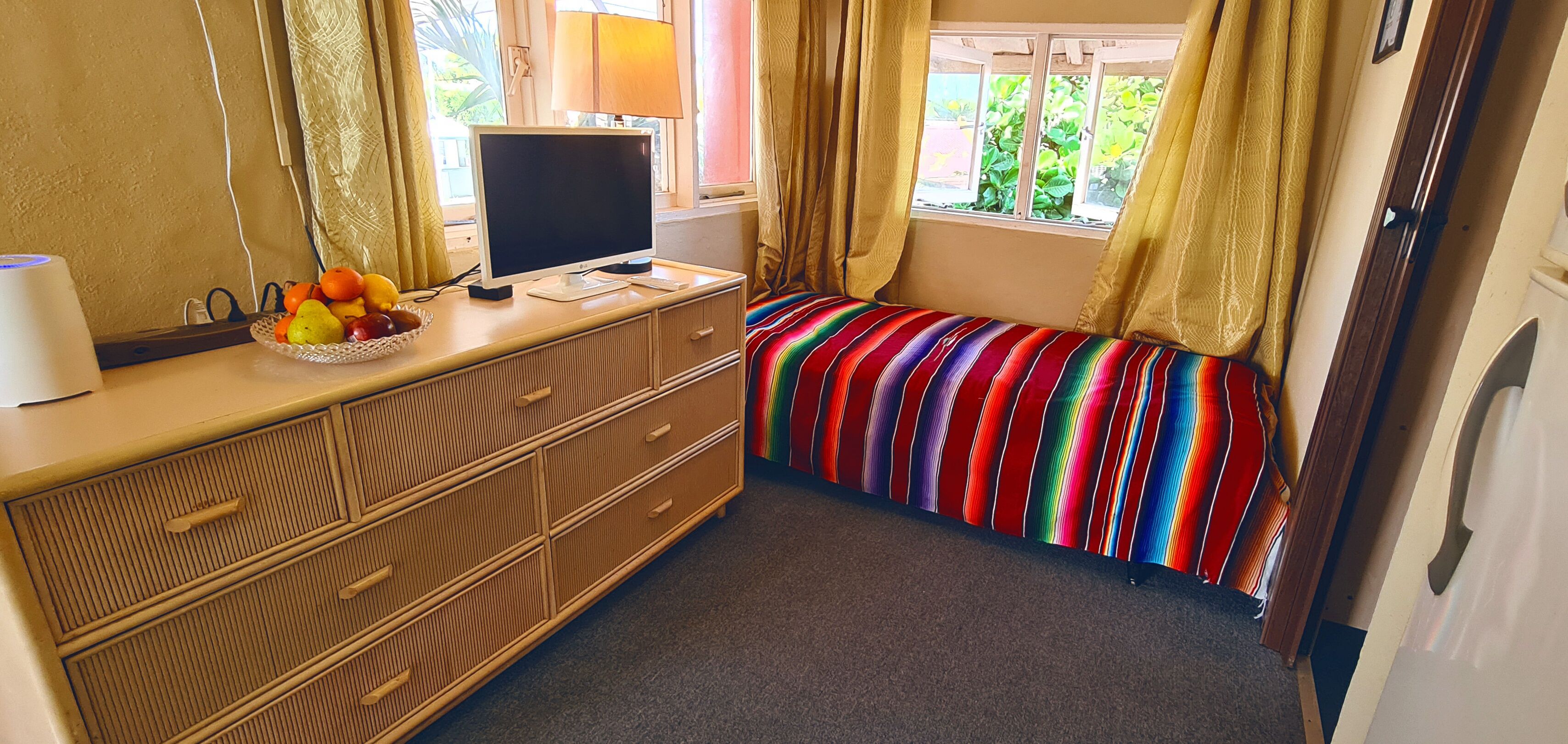 Quarto com cama, escrivaninha com computador, luminária e janela com cortinas.