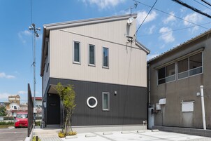 Um edifício moderno com telhado plano, porta de garagem e uma pequena árvore na frente.