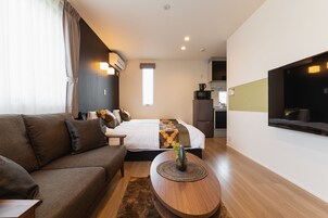 Quarto de hotel moderno com uma cama grande, um sofá, uma TV e uma cozinha compacta.