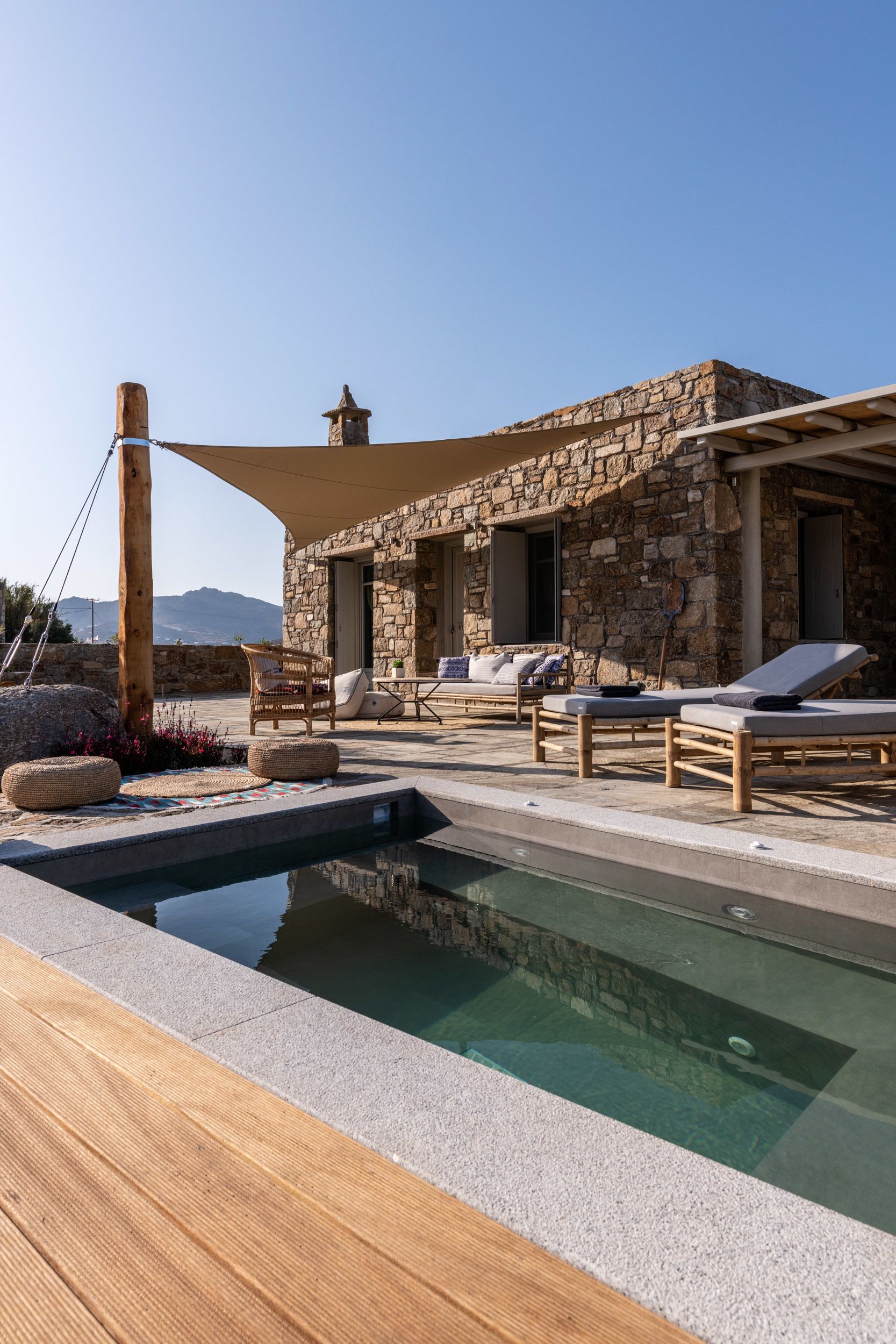 Um edifício de pedra com piscina, espreguiçadeiras e um deck de madeira.