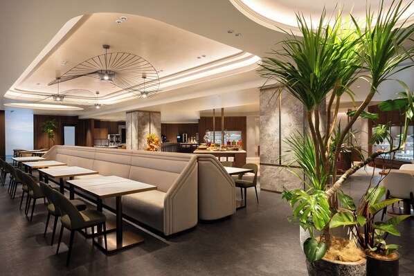 Um restaurante moderno com uma área de estar central, diversas mesas e uma variedade de plantas.