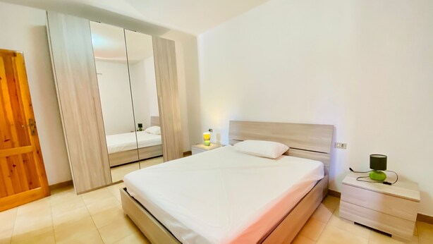 Quarto com cama, mesas de cabeceira, espelho e guarda-roupa.