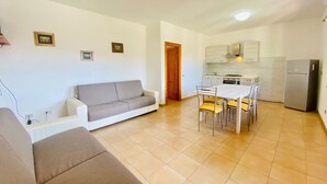 Espaço compacto para viver, com sofá, mesa de jantar, cadeiras, cozinha compacta e porta para outro cômodo.