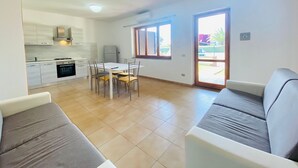 Uma cozinha moderna com armários brancos, uma mesa de jantar e cadeiras. Há um sofá e uma janela com vista para o exterior.