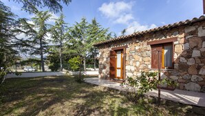 Uma casa de pedra com telhado em telhas, porta de madeira e um pequeno jardim com grama e árvores.
