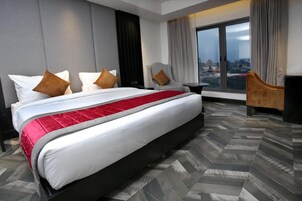 Quarto de hotel moderno com uma cama grande, vista da cidade pela janela e uma pequena mesa redonda.