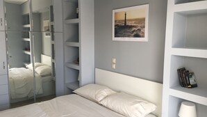 Quarto com cama, guarda-roupa, estante com livros e um quadro de um farol.