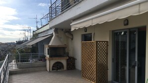 Um pátio no terraço com churrasqueira de tijolos, cerca de madeira e porta de vidro que dá para uma área coberta.