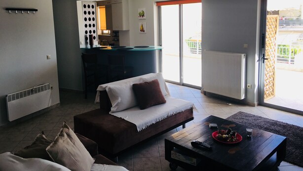 Sala de estar com sofá, mesa de centro e cozinha visível por uma porta aberta.