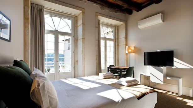 Quarto de hotel com uma cama grande, uma escrivaninha, uma cadeira, uma televisão e uma janela com cortinas.