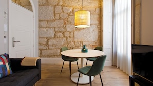 Uma sala de jantar com parede de pedra, uma mesa redonda, quatro cadeiras, um lustre, um sofá e uma televisão.