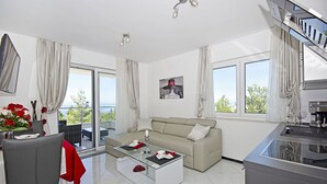 Uma sala de estar moderna com sofá, mesa de centro e área de jantar. Há uma escadaria à direita e uma varanda com vista.