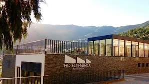 Hotel moderno com fachada de pedra e janelas amplas, situado contra um cenário montanhoso.