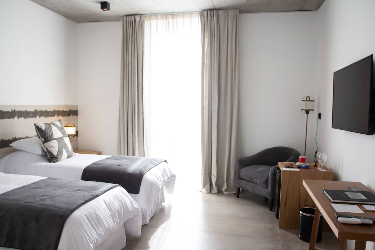 Quarto de hotel com duas camas, uma mesa de escritório, uma cadeira, uma televisão e uma janela com cortinas.