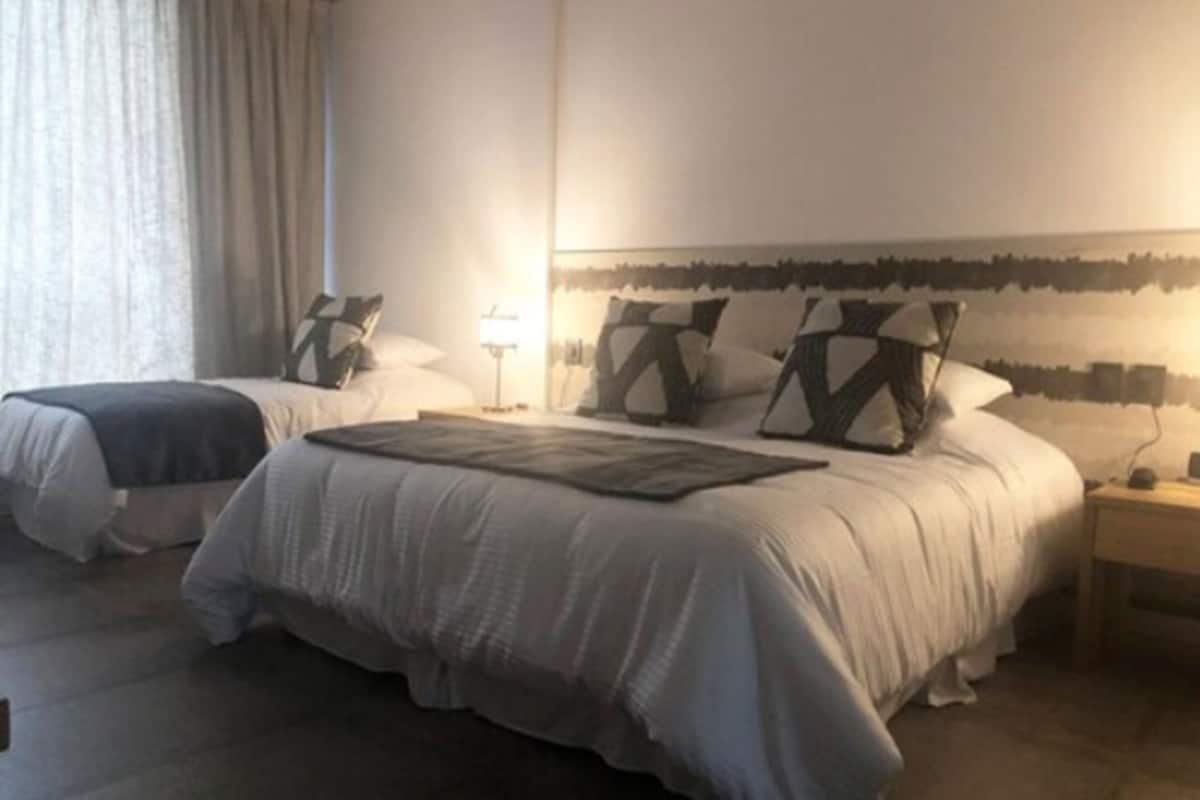 Quarto de hotel com duas camas, uma mesa de cabeceira com abajur e vista para o mar.