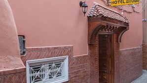 Um edifício rosa com porta de madeira e janela com grades decorativas.