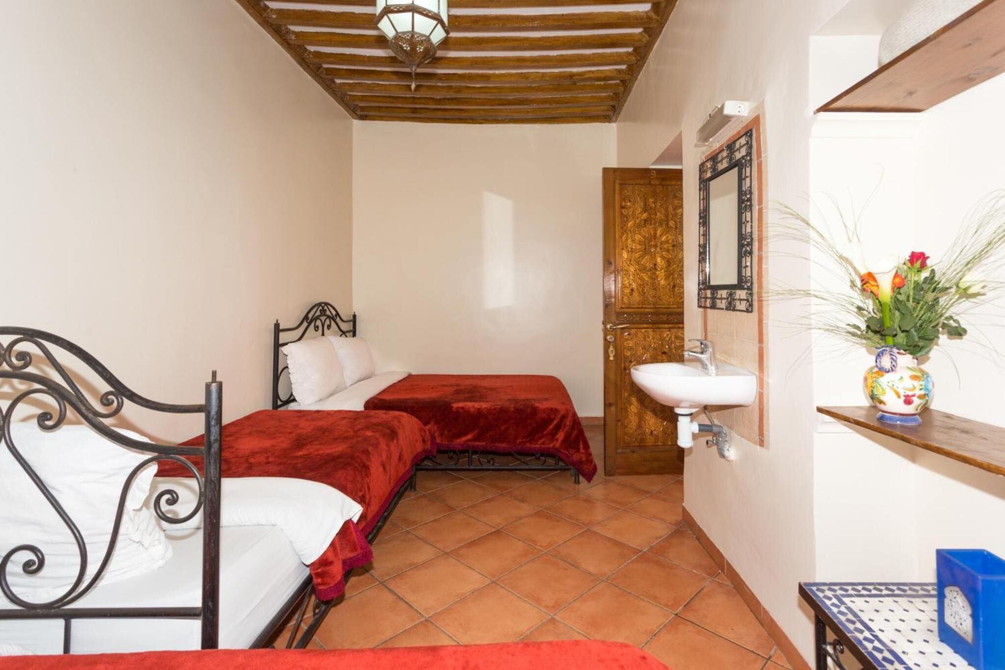 Quarto pequeno e aconchegante com cama, mesa de cabeceira, uma cadeira vermelha, pia e espelho.