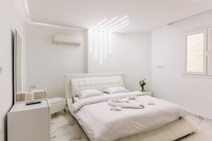 Quarto moderno com cama branca, mesa de cabeceira, ar-condicionado fixado na parede.