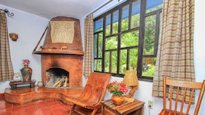 Quarto rústico com lareira de madeira, uma janela grande com cortinas, e uma cadeira de madeira.