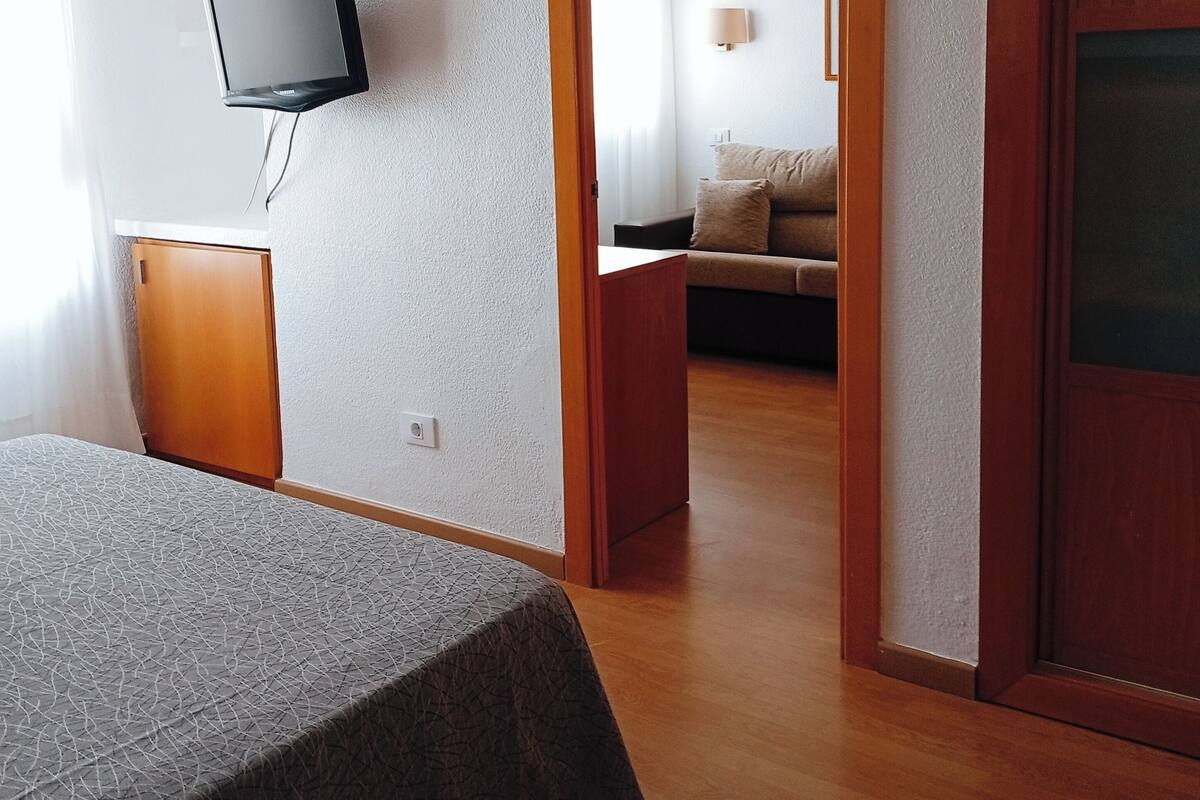 Quarto de hotel com cama, televisão na parede, porta de madeira e vista para a sala de estar.