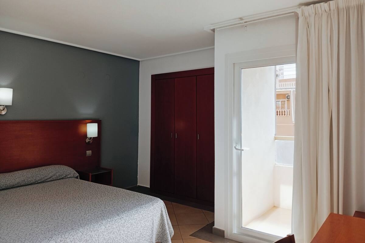 Quarto de hotel com cama, guarda-roupa, mesa de cabeceira e porta para uma varanda.