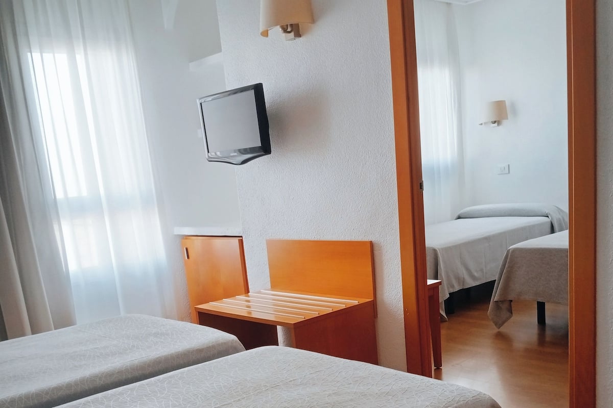 Quarto de hotel com duas camas, uma televisão presa à parede e uma cadeira de madeira.