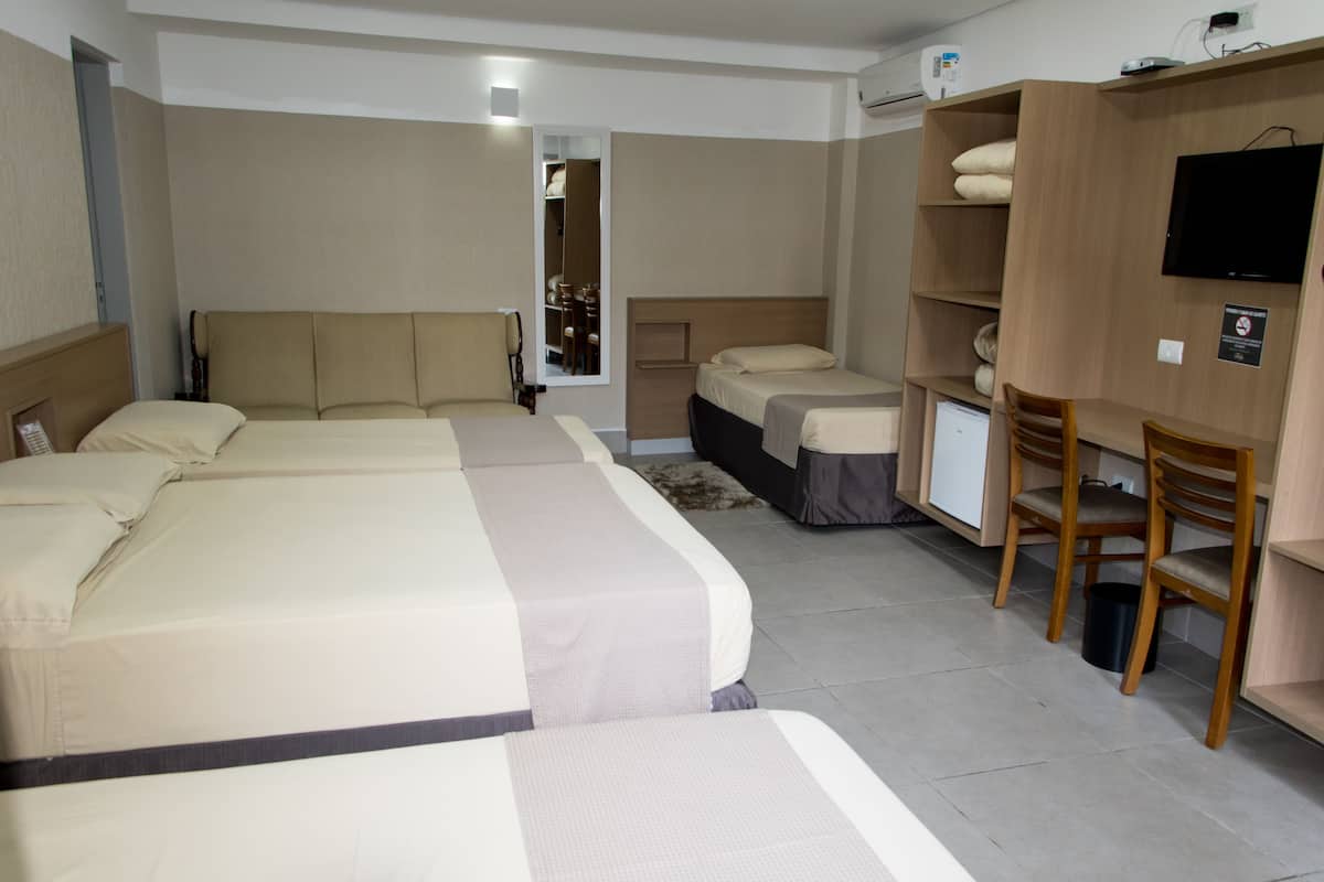 Quarto de hotel com três camas, uma escrivaninha e uma televisão.