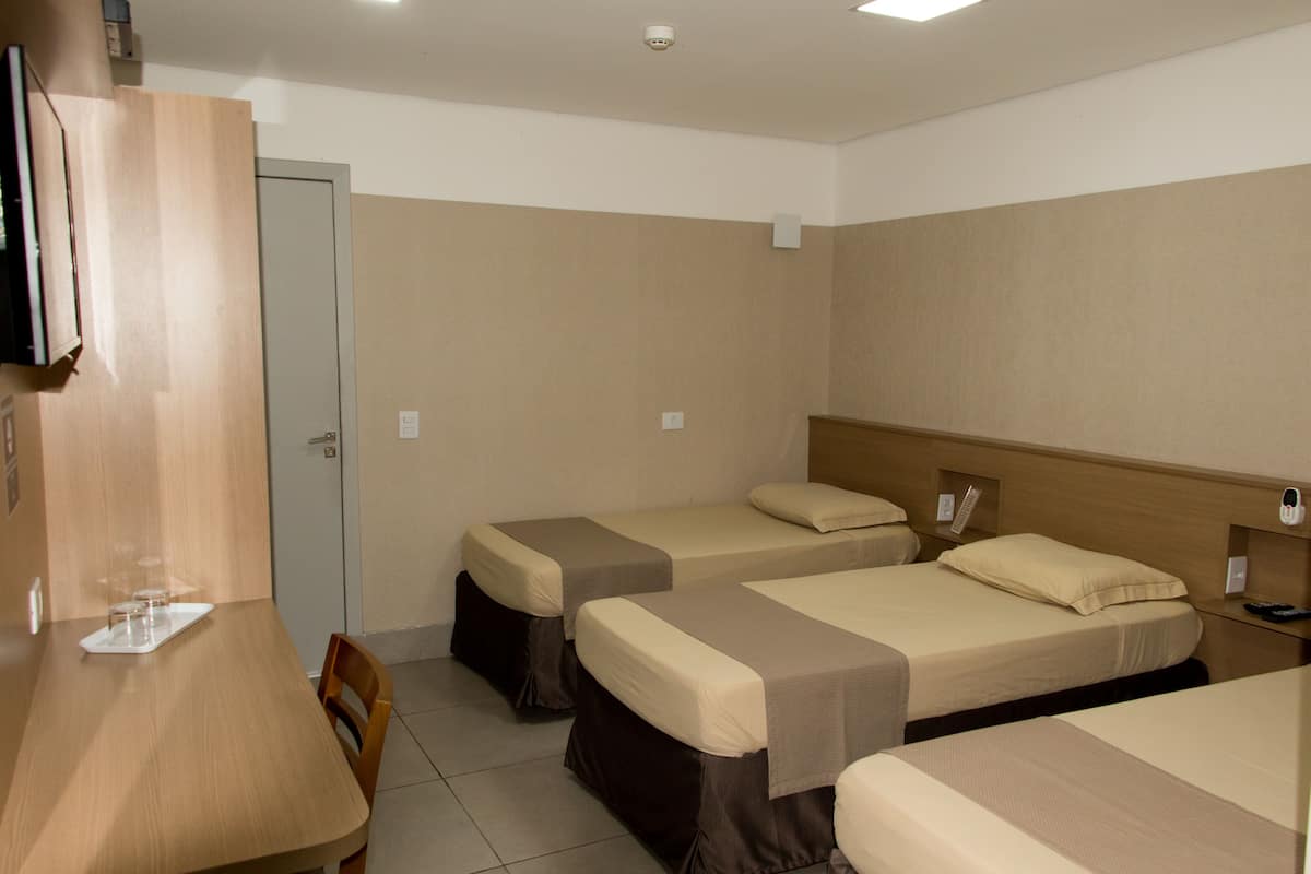 Quarto de hotel com duas camas de solteiro, uma escrivaninha de madeira e uma cadeira.