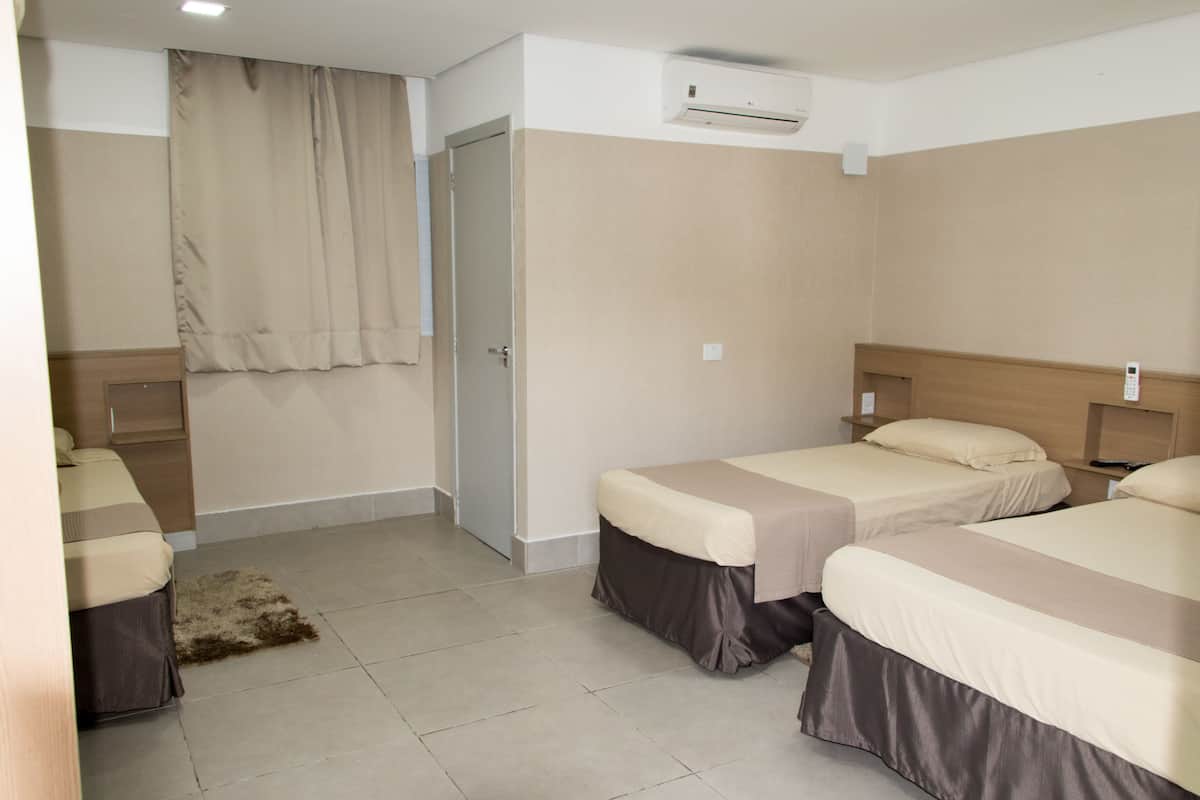 Quarto de hotel com duas camas, um tapete pequeno, uma porta e um ar condicionado.