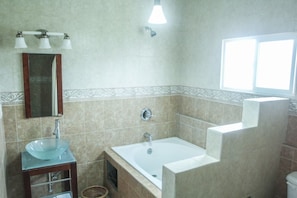 Casa de banho com lavatório de vidro, banheira e espelho.