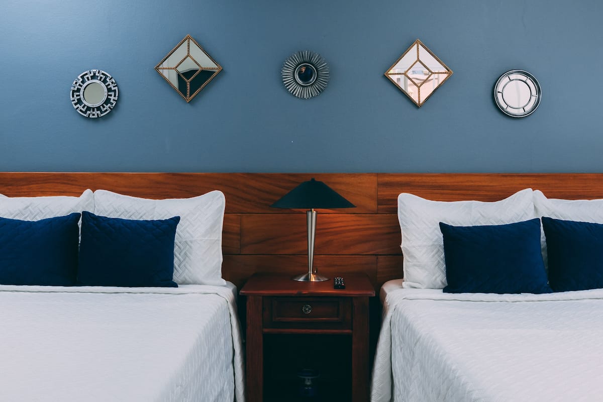 Quarto de hotel com duas camas, uma mesa de cabeceira e decoração na parede.