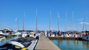Uma marina com vários veleiros atracados, um cais de madeira e diversos tipos de embarcações, incluindo jet skis.