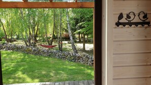 Uma porta de madeira com decoração de pássaro preto e vista para um jardim com uma rede e muro de pedra.